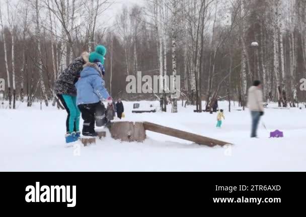 Girl helps her little brother to run on log during snowfall in winter ...