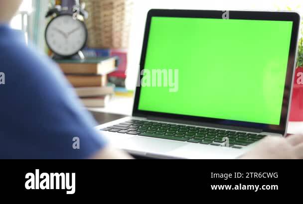 Over the shoulder view of young boy watching on laptop computer . Green ...