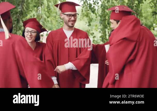 Slow motion of happy graduates wearing gowns and mortar-boards hugging ...