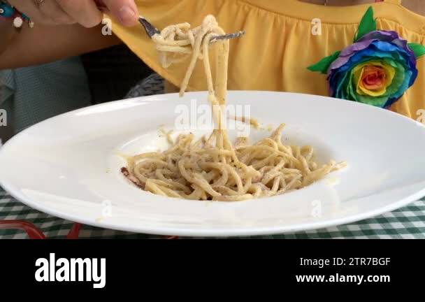 Woman in a yellow dress is eating a pasta with white sauce, by dint of ...