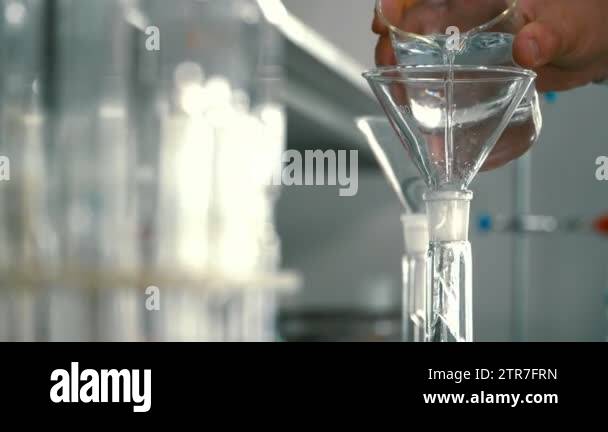 Chemist pouring alcohol into a flask through funnel. Scientist working ...