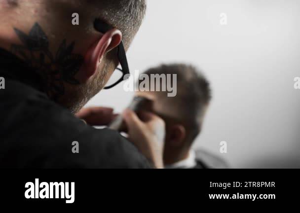 Tattoed barber makes haircut for customer at the barber shop by using ...