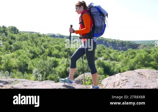 Girl hiker tourist with tracking sticks and backpack goes up mountain ...