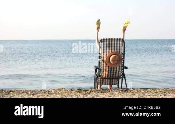 Rear view woman in beach chaise longue waving her flip-flops Stock ...