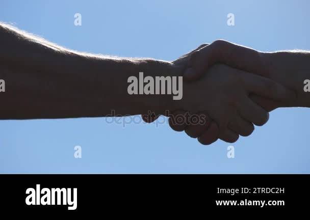 Friendly handshake of two unrecognizable muscular white men on blue sky ...