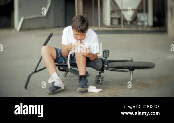 A young boy sits in a park after falling from a bike, calms the pain in ...
