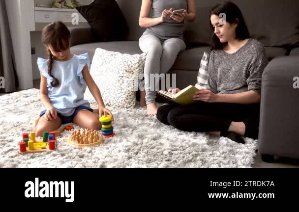 Young girl playing game with mother and asian nanny in living room ...