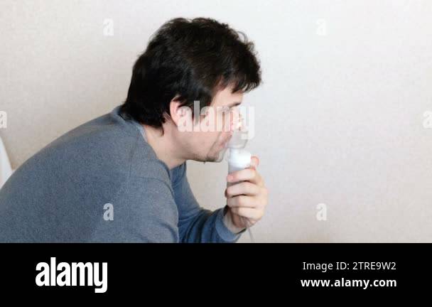 Use nebulizer and inhaler for the treatment. Young man inhaling through ...