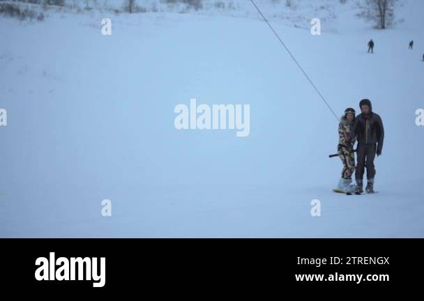 Two snowboarders on the ski resort rising up to the slope using the T ...