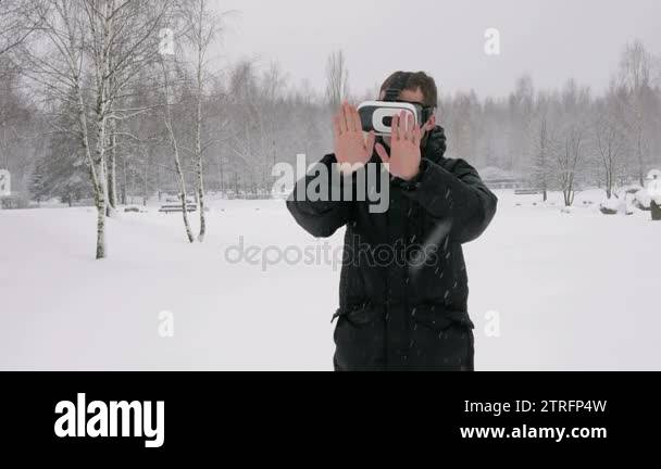 A man wearing a virtual reality headset in the winter in a snowy forest ...