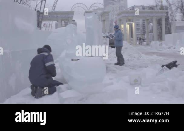 Worker using a chainsaw carving an ice sculpture. Men discuss work with ... Worker using a chainsaw carving an ice sculpture. Men discuss work with ...