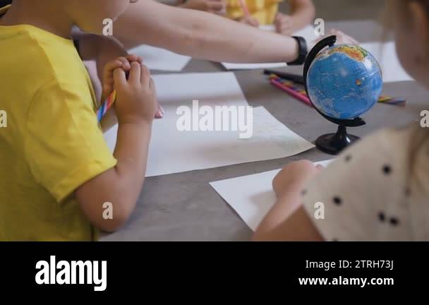 A group of children and a teacher draw on white paper using colored ...