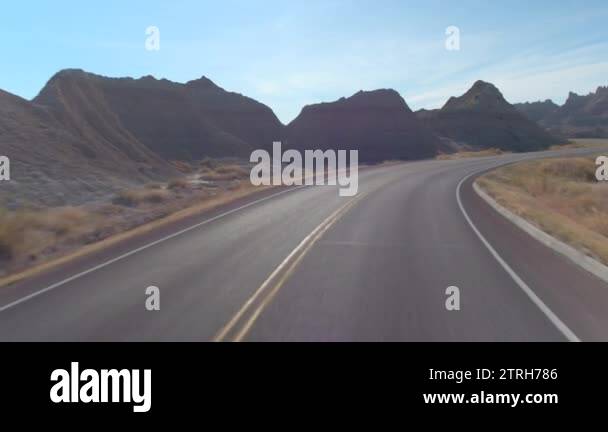 FPV: Driving along the empty road snaking through picturesque Badlands landscape with rocky ...