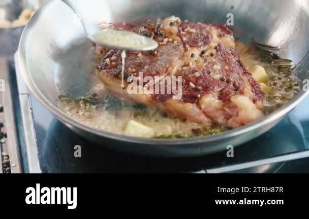 Meat steak is fried in butter and grease on frying pan, close-up in ...