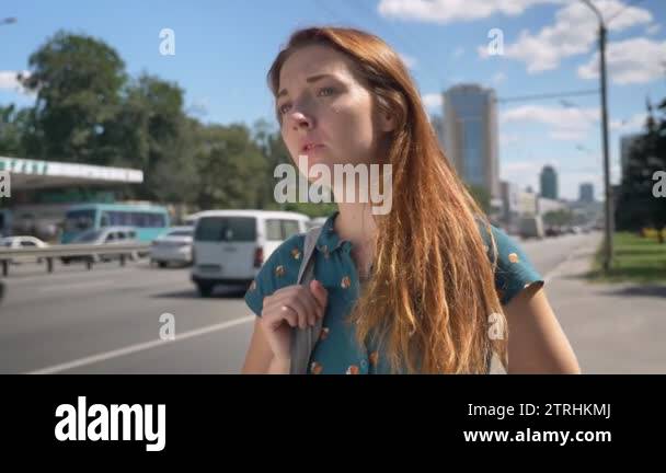 Concerned ginger young woman waiting for taxi and standing on urban ...