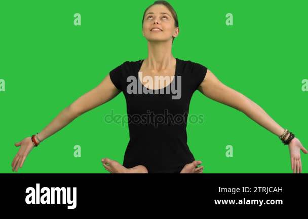 Young woman sitting in lotus yoga pose practicing meditation on a Green ...