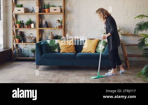 Attractive young woman is cleaning living room mopping the floor doing ...