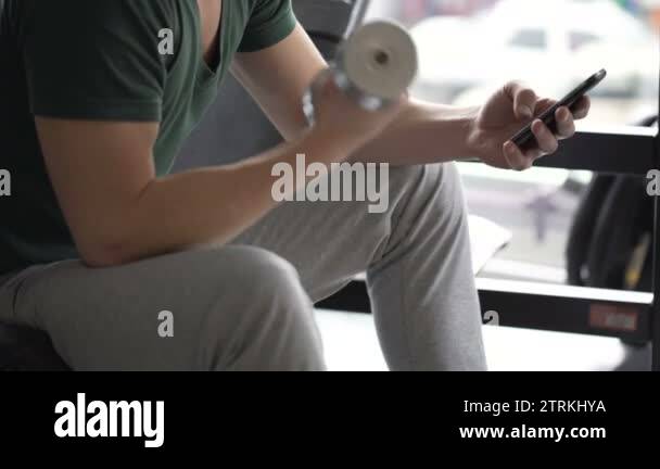 Muscular athlete doing dumbbell exercise, checking workout routine on ...