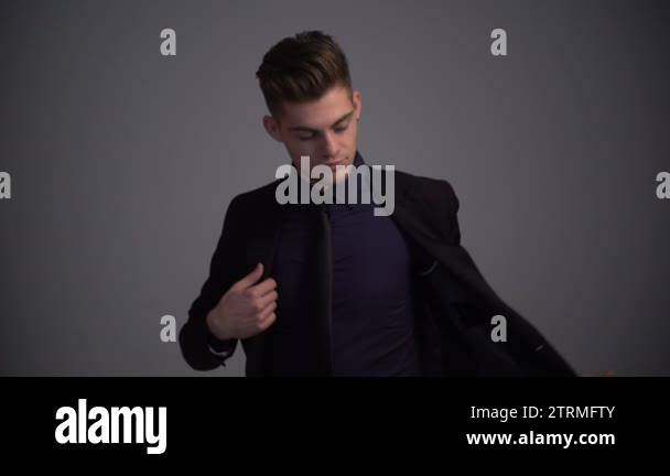 Handsome guy in a blue shirt, takes off his jacket in a studio. Young ...
