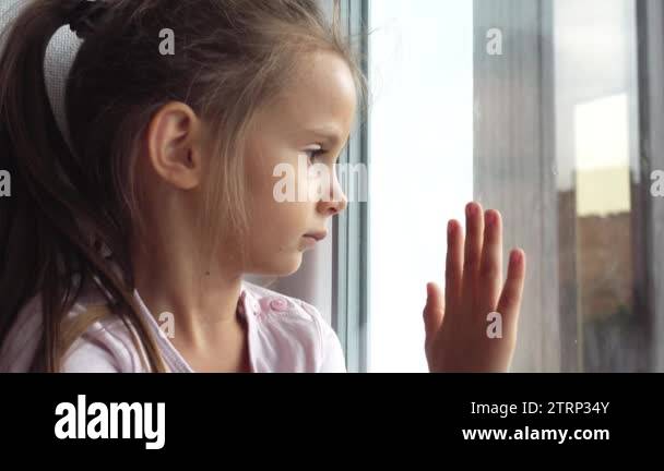 Portrait of a small sad girl by the window. Sad child looks out the ...