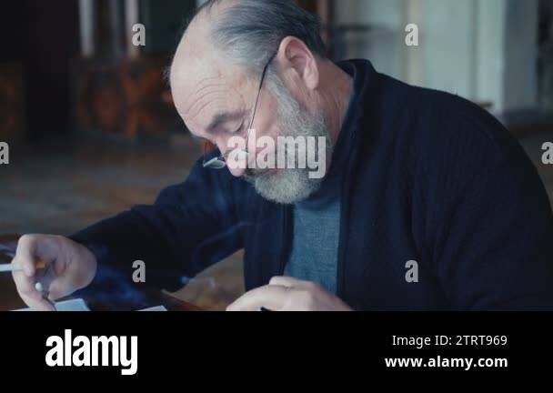 Emotional tired old man smoking cigarette, sighing and working with ...