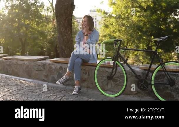 Pretty girl sitting on the bench or parapet in the city park with her ...