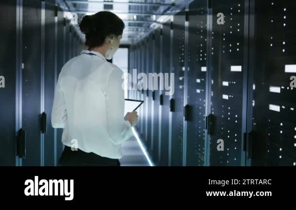 Female Server Technician Walking in Data Center Corridor with Rows of Rack Servers. She's ...