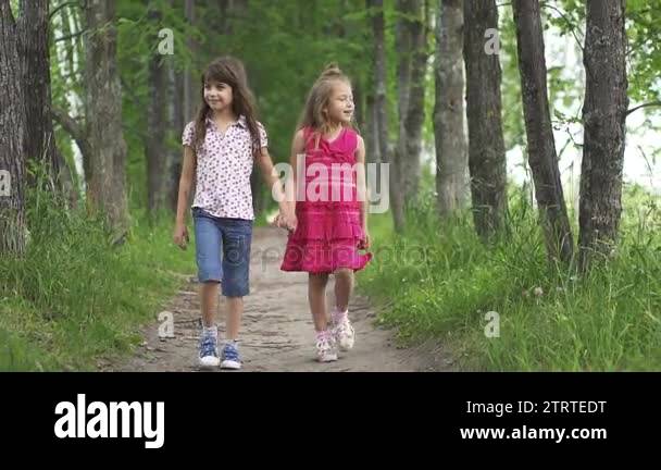 two little girls hold hands and walk down the green alley. children ...