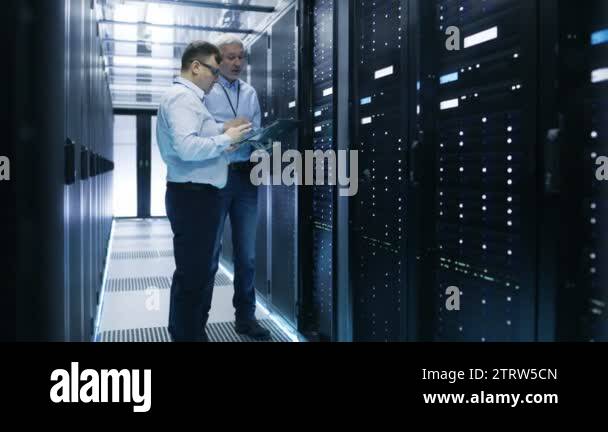 Two IT Engineers Standing in Working Data Center. They Use Laptop and ...