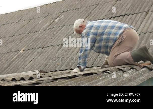An elderly man is fixing the roof himself. Old wooden house in slate ...