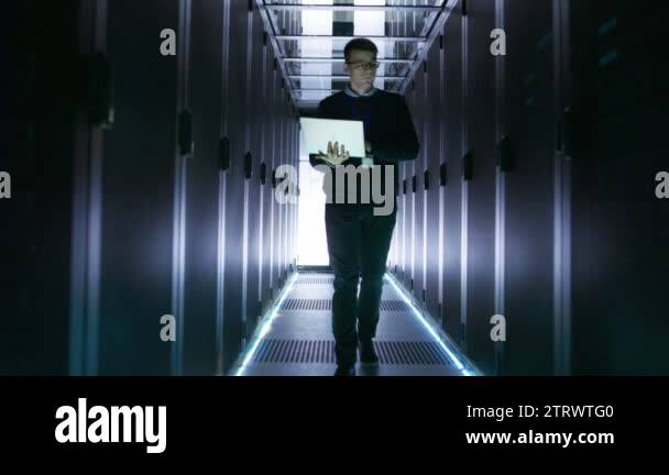 Male Server Engineer Walks with Open Laptop Through the Rows of Rack ...