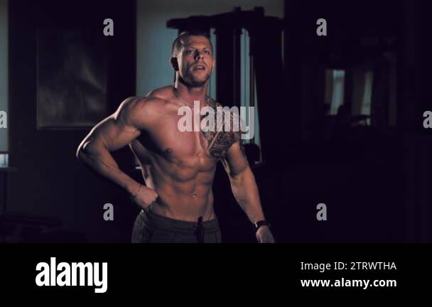 Young bodybuilder with a bare torso posing in a gym. 60 to 24fps 4K ...