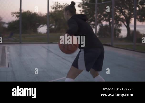Backside footage of a young basketball female player jogging with ball ...