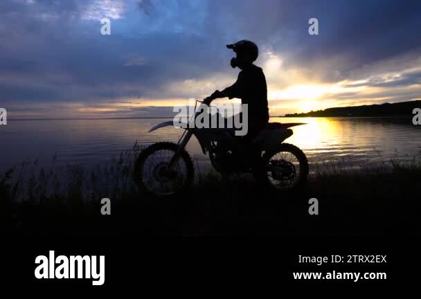 Motocross rider starting engine in his enduro bike. Sunset, sky and ...