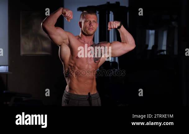 Young bodybuilder with a bare torso posing in a gym. 60 to 24fps 4K ...
