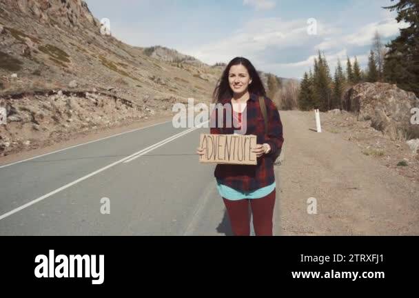 Teenage Girl Holding An Adventure Sign On A Mountain Road, Smiles And ...