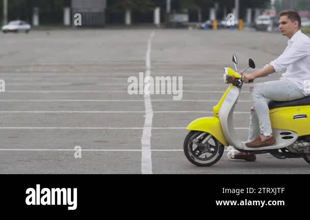 Guy on the scooter starts driving in the parking lot. Young man riding ...