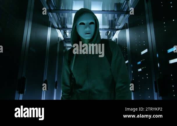 Masked Hacker in a Hoodie Walks Through Corporate Data Center with Rows ...