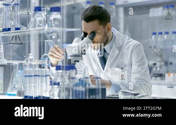 Young Male Research Looks at Sample under Microscope then Looks into ...