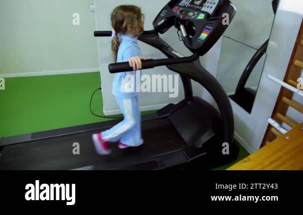 Little girl walks by treadmill and looks to panel with hands on ...