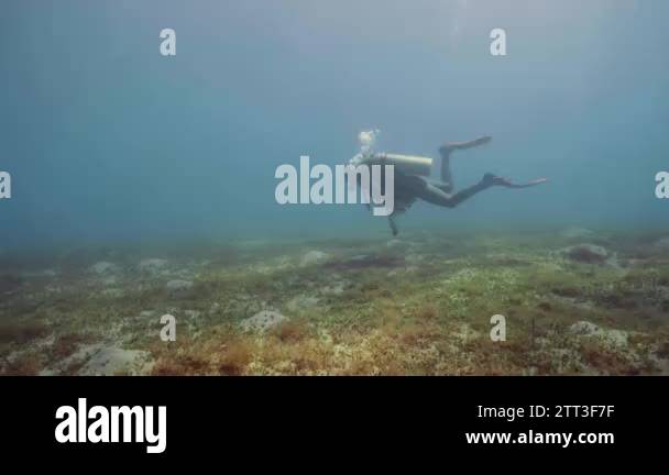 Scuba diver floating on sea bottom and waving hand to camera ...