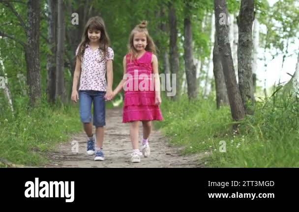 two little girls hold hands and walk down the green alley. children ...