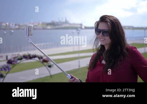 Young beautiful girl is making a photo on a selfie stick on a ...