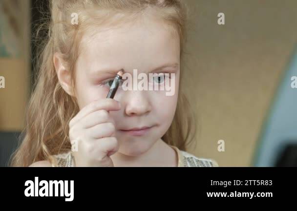 little girl with red hair draws eyebrows with eyebrow pencil, looks in ...