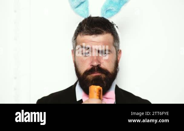 Bearded man wearing a suit and with ears of a rabbit eat carrots and ...