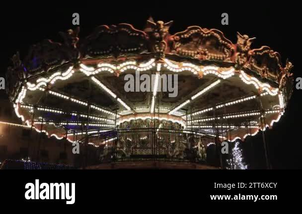 Illuminated vintage fairground carousel with wooden horses rotating at ...
