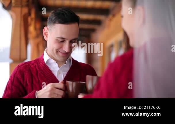 Groom and bride drink coffee or tea out of cups on a balcony of wooden ...