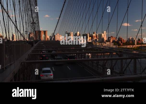 Cars riding and pedestrians walk over the Brooklyn Bridge at sunset ...