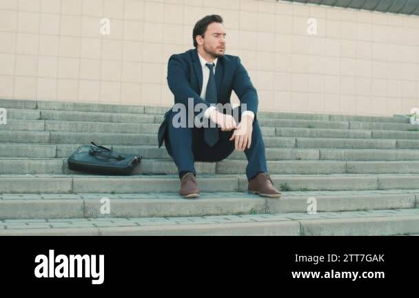 Young businessman sitting on the stairs near office building, feeling ...