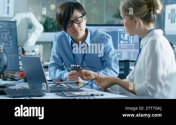 Two Computer Engineers Talking, They Connect Printed Circuit Board to a Laptop and Start Coding ...